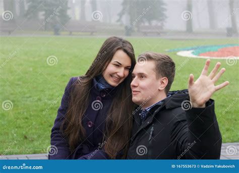 Девушка сидит на коленях у молодого человека Смех и жесты парня На скамейке в туманном парке