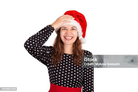 혀를 표시 하 고 아래를 내려다 보면서 멋진 즐거운 여자는 머리에 손을 웃는 다 산타 클로스에 감정적인 여자 크리스마스 모자 흰색 배경에 고립 휴일 개념 12월에 대한 스톡