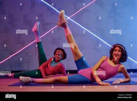 Young Caucasian And African American Girls Doing Side Leg Raise Exercise On Floor At Gym Stock