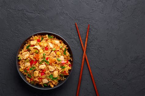 어두운 슬레이트 배경에 검은 그릇에 Schezwan 치킨 볶음밥 사천 쌀은 피망 녹색 콩 당근 닭 가슴살을 곁들인 인도 중국 요리 요리입니다 공간을 복사합니다 맨 위 보기