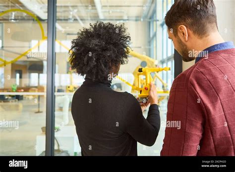 Two Engineers Collaborate On Programming A Robotics Arm In A Modern