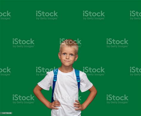 배낭을 메고 흰 티셔츠를 입은 소년이 허리에 손을 얹고 있다 텍스트를 위한 공간이 있는 녹색 배경입니다 선택적 초점 6 7 살에 대한 스톡 사진 및 기타 이미지 Istock