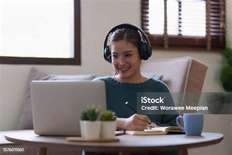 젊은 아시아인은 집에서 노트북으로 휴식을 취하며 웃고 있는 예쁜 여자를 편안하게 지었다 아늑한 소파에서 휴대폰으로 즐기는 기쁨을 느끼는 여성 보기 정적 활동에 대한 스톡