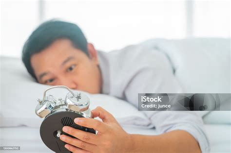 침대에서 자고있는 지친 남자는 불면증으로 고통받는 아침에 알람 시계 링에 깨어나피곤합니다 30 34세에 대한 스톡 사진 및 기타