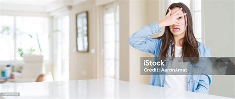 집에서 하얀 탁자 위에 앉아 얼굴과 눈을 손으로 덮고 부끄러운 표정으로 손가락을 들여다보는 아름다운 젊은 여성의 광각 사진 가리기에 대한 스톡 사진 및 기타 이미지 Istock