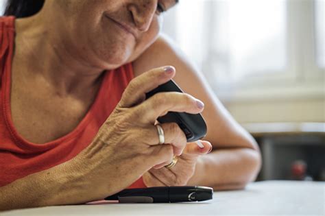 제1형 당뇨병을 앓고 있는 자신감 넘치는 백인 중년 여성이 부엌에 앉아 혈당 수치를 확인하기 위해 혈당 측정기로 루틴을 수행하는 클로즈업 샷 50 54세에 대한 스톡 사진