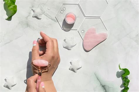 핑크 쿼트 페이스 롤러 구아 샤 스톤 유리 항아리에 핑크 크림 흰색 플랫은 녹색 얼음과 이국적인 고사리 잎과 분홍색 색상에 누워 뷰티 핸드 마사지 잘 손질 된 손톱을 가진