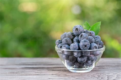 玻璃高清图片 蓝莓叶放在木桌上的玻璃碗里夏天静物木桌上的玻璃碗里有叶子的蓝莓 餐饮美食免费下载 jpg格式 4084像素 编号