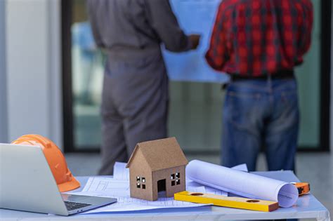 노란색 옷을 입은 두 명의 엔지니어가 하얀 그랜드 플랜 문서를 논의하고 있다 두 명의 동료가 사무실의 책상에서 건설 현장에서