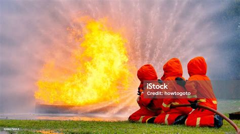 소방관 구조 팀 소방 소화기 훈련 소방 호스 화학 물 거품 스프레이 엔진을 사용하여 화염과 싸우는 소방관 팀워크 소방관은 하드 모자 안전 복 유니폼을 착용합니다 건물 외관에