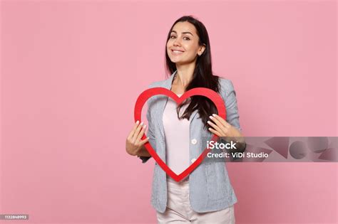 스튜디오에서 분홍색 파스텔 벽 배경에 고립 된 큰 빨간 나무 심장 지주 줄무늬 재킷에 쾌적 한 꽤 젊은 여자의 초상화 사람들은 진심으로 감정 라이프 스타일 개념입니다 복사