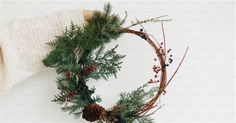 흰색 배경에 여성 손에 소박한 크리스마스 화환 세련된 니트 스웨터를 입은 여자는 전나무 가지 열매 원뿔 휴일 강림으로 현대 크리스마스 화환을 들고 있습니다 사진