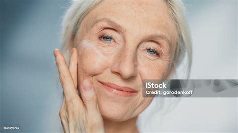 얼굴 크림을 부드럽게 바르는 아름다운 시니어 여성의 초상화 노인 여성은 천연 안티 에이징 화장품으로 피부를 부드럽고 매끄럽고 주름이 없습니다 뷰티 스킨케어 메이크업 용 제품