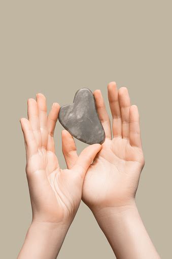 베이지 색 배경에 갈색 옥 구아 샤 스크레이퍼와 여성 모델 손 스파 바디 케어 도구 뷰티 케어 구아 샤 돌 스크레이퍼 공간을 복사합니다 괄사에 대한 스톡 사진 및 기타