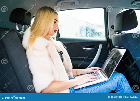 Красивая бизнес леди использует компьтер книжку и усмехается пока сидящ на заднем сиденье в