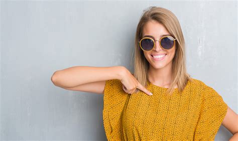 아름 다운 젊은 여 자가 자신에 게 놀라운 얼굴 가리키는 손가락으로 복고풍 선글라스를 착용 하는 그런 지 회색 벽을 통해 서 가리키기에 대한 스톡 사진 및 기타 이미지