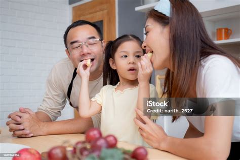 부엌에서 아버지 어머니 딸과 함께 행복한 가족 딸이 집에서 함께 사과 과일을 먹이고 엄마 아빠 아이는 유대감과 관계 생활 방식과 영양 개념을 가지고 있습니다 3 명에 대한