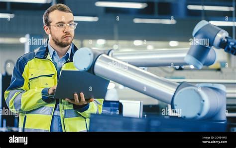 At The Factory Automation Engineer Uses Laptop For Programming Robotic