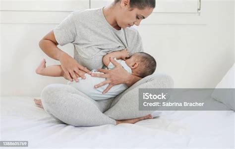 젊은 사랑하는 엄마는 침실 내부 그녀의 6 개월 된 아기를 모유로 기르고 어머니와 아이 사랑 유아를 들고 어머니의 손에 초점을 맞춥니다 모유 수유에 대한 스톡 사진 및 기타