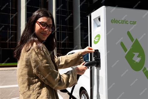 전기 자동차를 충전하는 측면 보기 웃는 여자 무료 사진