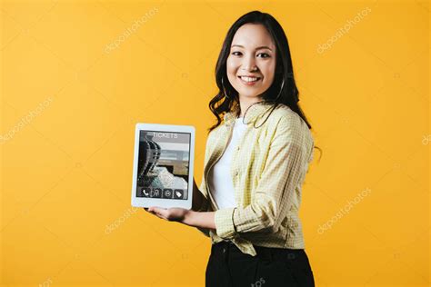 feliz asiático chica mostrando digital tablet con tickets aplicación aislado en amarillo