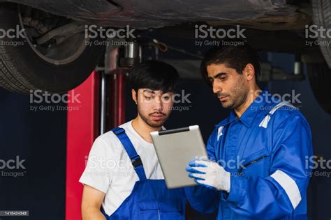 유니폼을 입고 태블릿을 사용하고 수리 수리 자동차 또는 자동차 부품 점검 또는 검사 자동차 유지 보수 서비스 센터 또는 상점에서 일하는 두 명의 잘 생긴 남성 정비사 산업