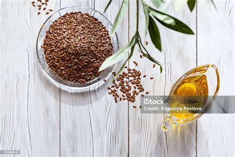 아마씨 오일과 흰색 나무 테이블에 아마 씨앗의 무리 오일과 아마씨 올리브 가지 및 복사 공간이있는 현대 의 정물 유리 그릇