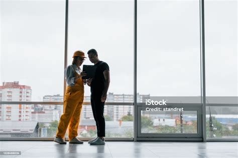 노란 유니폼과 단단한 모자를 쓰고 남자와 함께 실내에 서 있는 여성 노동자 또는 엔지니어 남자에 대한 스톡 사진 및 기타 이미지