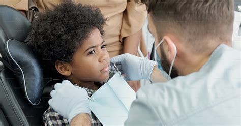 구강 검사 전에 작은 환자의 가슴에 냅킨을 씌우는 유니폼 장갑 보호 마스크를 쓴 젊은 치과 의사 사진 Unsplash의 건강한 라이프 스타일 이미지