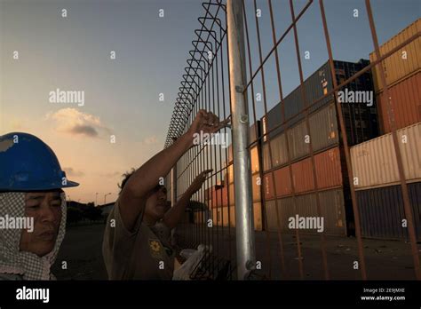 Workers Running Maintenance Activity On The Fencing Of A Container Terminal Area Which Is The