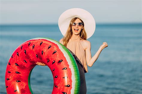 수영복을 입고 풍선 수영 원으로 바다에 누워있는 여름 모자를 쓴 흥분한 행복한 소녀는 행복하고 승리의 제스처를 보여줍니다 여름 방학 여행 가냘픈에 대한 스톡 사진 및 기타