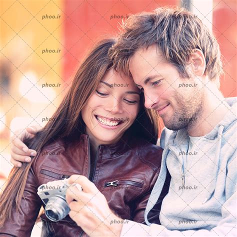 عکس با کیفیت زوج جوان خندان در حال نگاه کردن به عکس های داخل دوربین