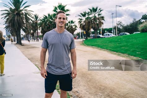 쾌활한 백인 힙스터 남자의 절반 길이 초상화는 아침 듣기 음악에서 훈련을 받고 이어폰을 사용하여 피트니스 목표를 달성하기 위한 동기 부여 음악을 즐기는 웃는 스포츠맨의