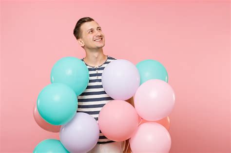 밝은 동향 분홍색 배경에 고립 된 다채로운 공기 풍선 들고 줄무늬 티셔츠를 입고 매혹적인 젊은 행복 한 남자의 초상화 사람들이 진심으 감정 라이프 스타일 개념 광고