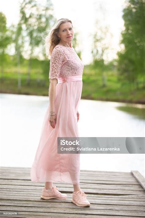 흐르는 분홍색 드레스를 입은 아름다운 노인 여성이 강 근처의 나무 다리에 서 있습니다 50 54세에 대한 스톡 사진 및 기타 이미지 50 54세 개발 건강한 생활방식