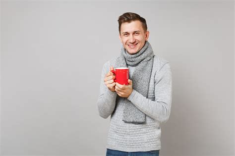 회색 스웨터에 젊은 남자가 미소 커피 또는 차 스튜디오에 회색 배경에 고립의 빨간 컵을 들고 스카프 건강 한 라이프 스타일 아픈