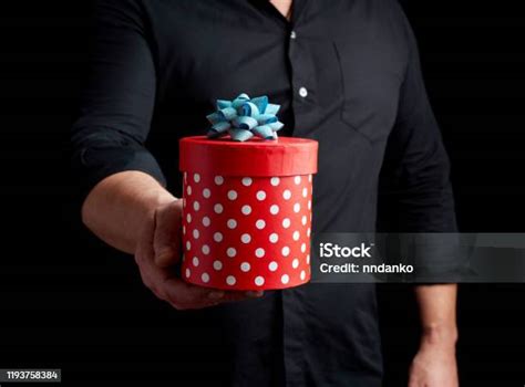 검은 셔츠를 입은 성인 남성이 파란색 활이 달린 둥근 빨간 물방울 무늬 상자를 손에 들고 있습니다 개념에 대한 스톡 사진 및 기타 이미지 Istock