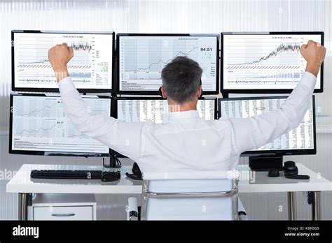 Rear View Of Successful Stock Market Trader Looking At Graphs On
