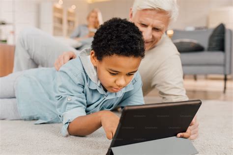 고위 아빠와 귀여운 다인종 아이의 행복한 가족은 바닥에 누워 태블릿으로 휴식을 취하고 즐거운 시간을 보내고 있습니다 집에서