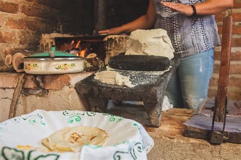 Mexican Female Preparing Corn Mace On A Metate And A Wood Stove To Make