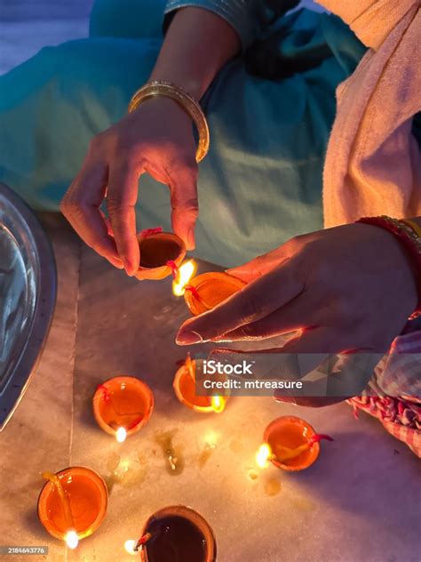 대리석 바닥 조명에 다리를 꼬고 앉아있는 알아볼 수 없는 여자의 클로즈업 이미지 기름으로 가득 찬 미티 클레이 디야 어둠 속에서 깜박이는 불꽃 빛의 디왈리 축제 축하 높은
