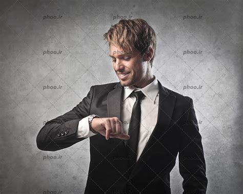عکس با کیفیت مدل مرد با چهره ی جذاب و کت و شلوار مشکی در حال نگاه کردن به ساعت خود عکس با