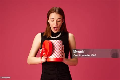 놀라게 하다 검은 드레스를 입은 젊은 아름 다운 여자 축하 분홍색 스튜디오 배경에 대한 오프닝 선물 20 24세에 대한 스톡