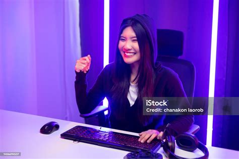 비디오 게임을합니다 거실에 컴퓨터 Pc가있는 의자에 앉아있는 젊은 아시아 예쁜 여자 행복한 여성 전문 스트리머 중국 착용 까마귀 놀이 게임 어두운 방 네온 빛에서 온라인으로