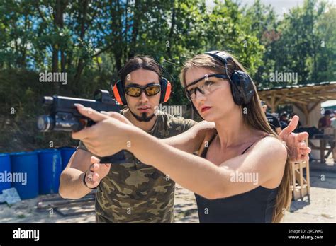 Male Instructor In Camo T Shirt Guiding Female Client Operating Handgun Safety Headphones And