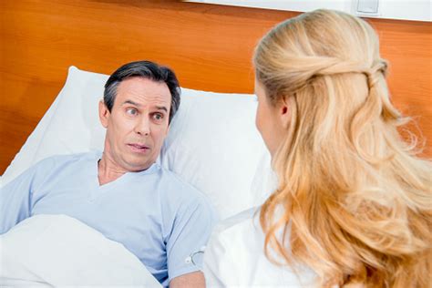 침대에 누워 있는 중년 환자와 병원에서 그 근처에 앉아 있는 의사 건강관리와 의술에 대한 스톡 사진 및 기타 이미지 건강관리와 의술 남자 노인 Istock