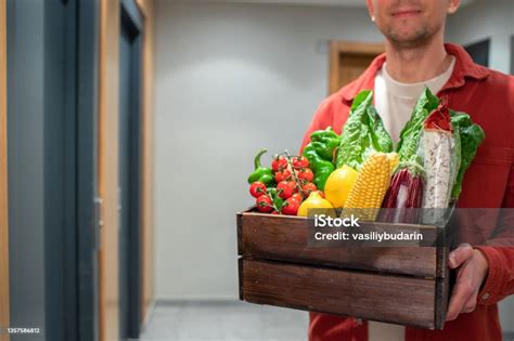 현관에 음식과 종이 봉투를 들고 배달 남자 택배는 고객에게 신선한 야채와 과일이있는 상자를 제공합니다 30 34세에 대한 스톡