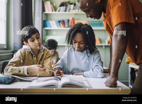 Side View Of Teacher Assisting Students Studying In Classroom Stock