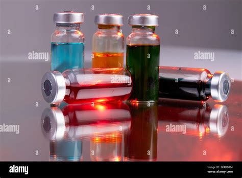 Collection Of Drug Vials With Colored Solution Vaccine Bottles On Reflective Surface Stock
