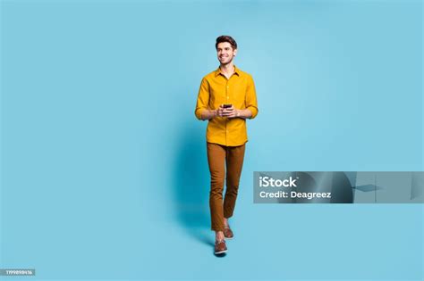 파스텔 색상 배경을 통해 고립 된 바지 바지를 입고 당신을 향해 움직이는 이빨로 움직이는 손에 들고 있는 쾌활한 잘생긴 남자의 전체 길이 바디 사이즈 사진 남자에 대한 스톡